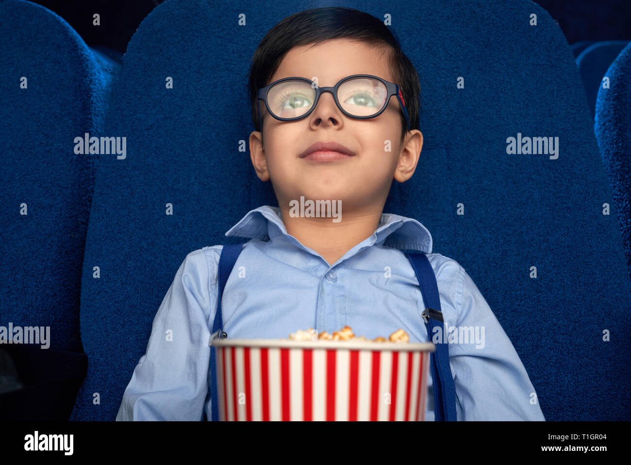 Front view of cute, little boy enjoying movie premiere. Cheerful kid ...