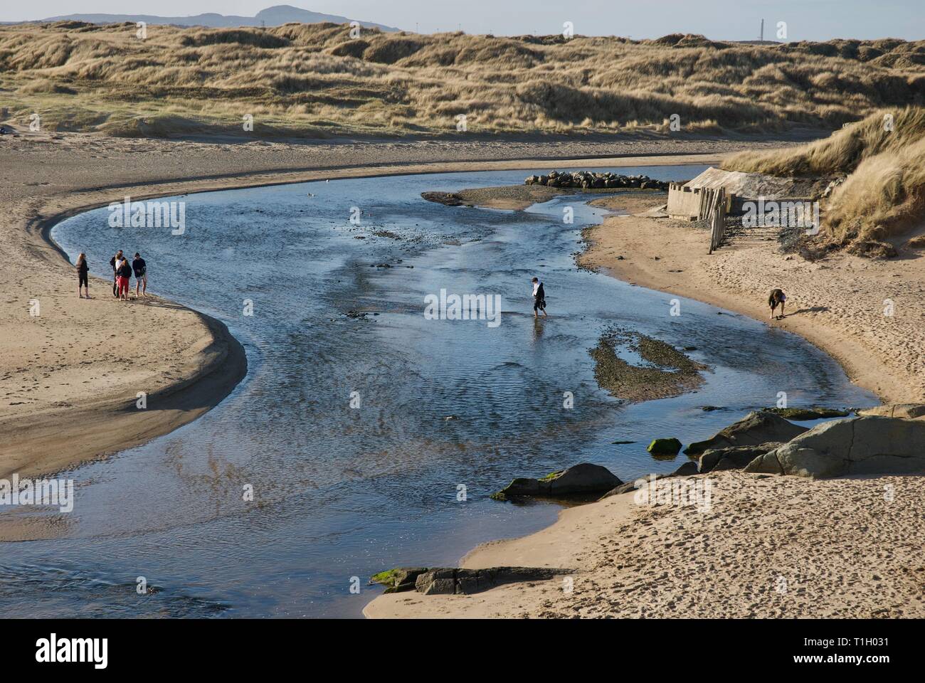 Distant figures wade across the Afon Crigyll river, Rhosneigr, Anglesey ...