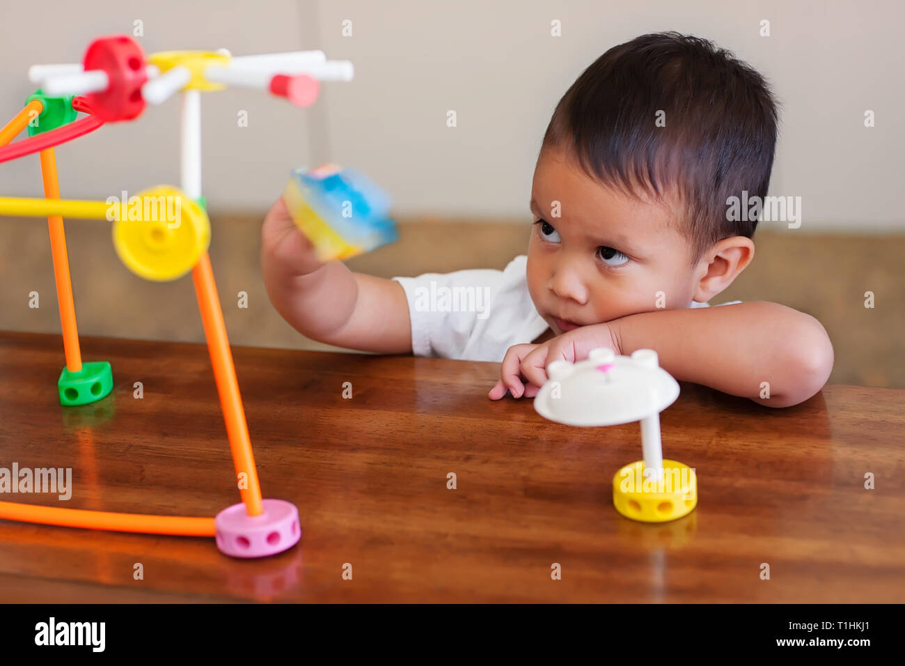 A moody child playing alone with learning toys on a table and ...