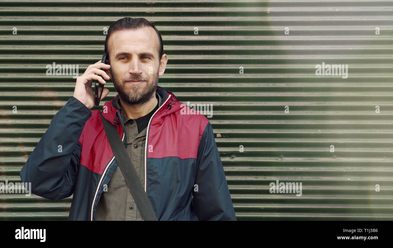 Young man standing against a wall background and talking on the ...