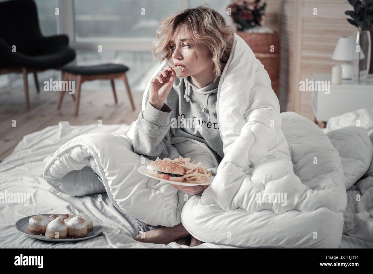 Sad and lonely woman eating burger and French fries in the bed Stock ...
