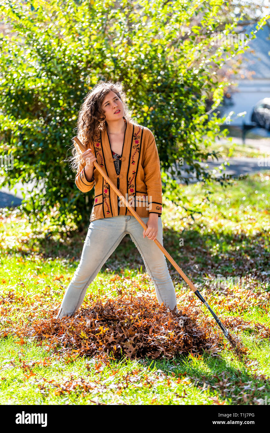 Young woman homeowner in garden front yard backyard raking collecting ...
