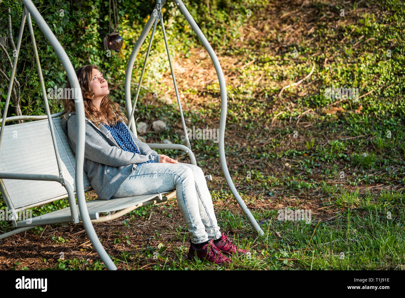 Young smiling woman sitting on garden swing in morning, happy, enjoying ...