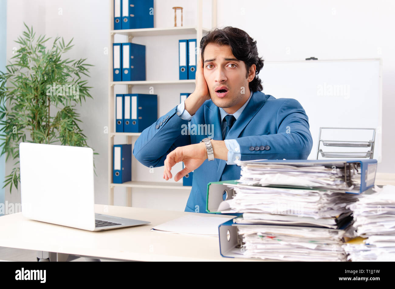Young handsome male employee with too much work in the office Stock ...