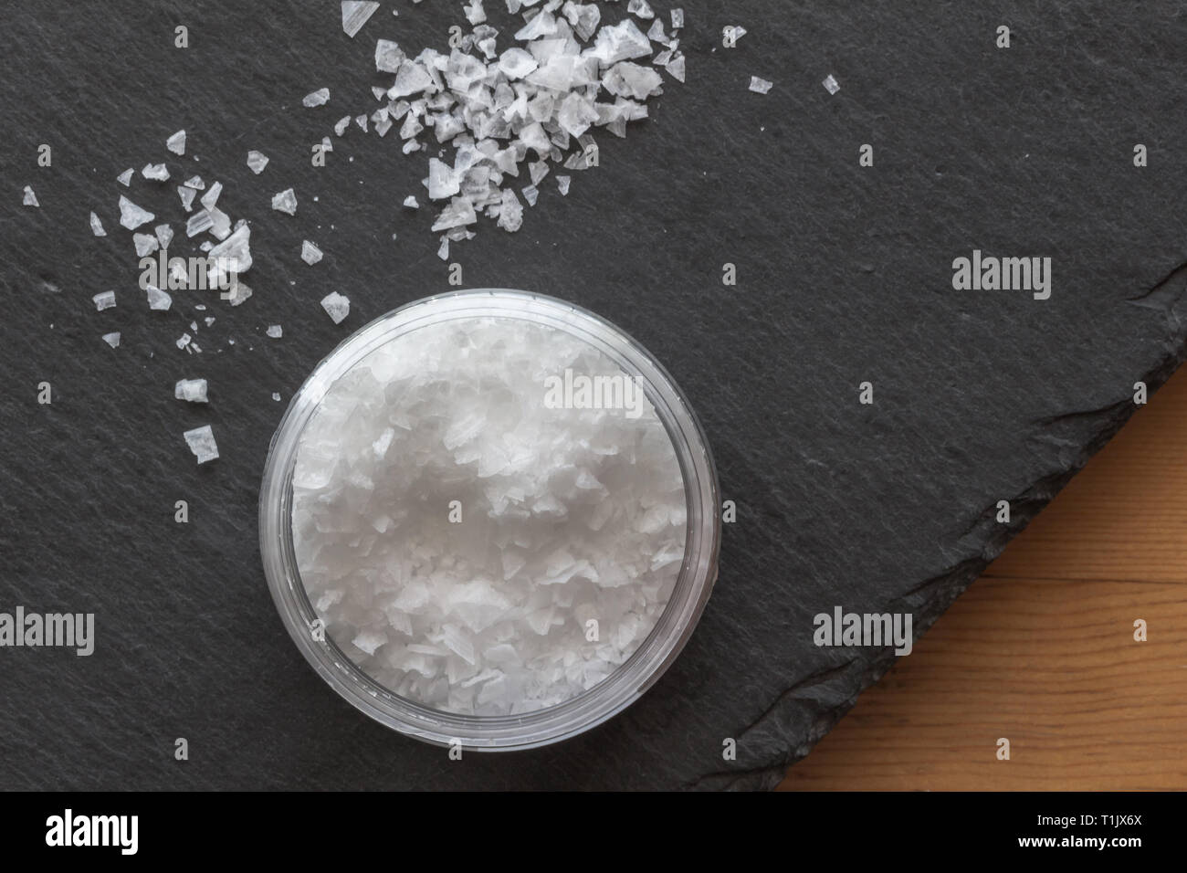 Salt in a container with salt flake crystals on black slate background ...