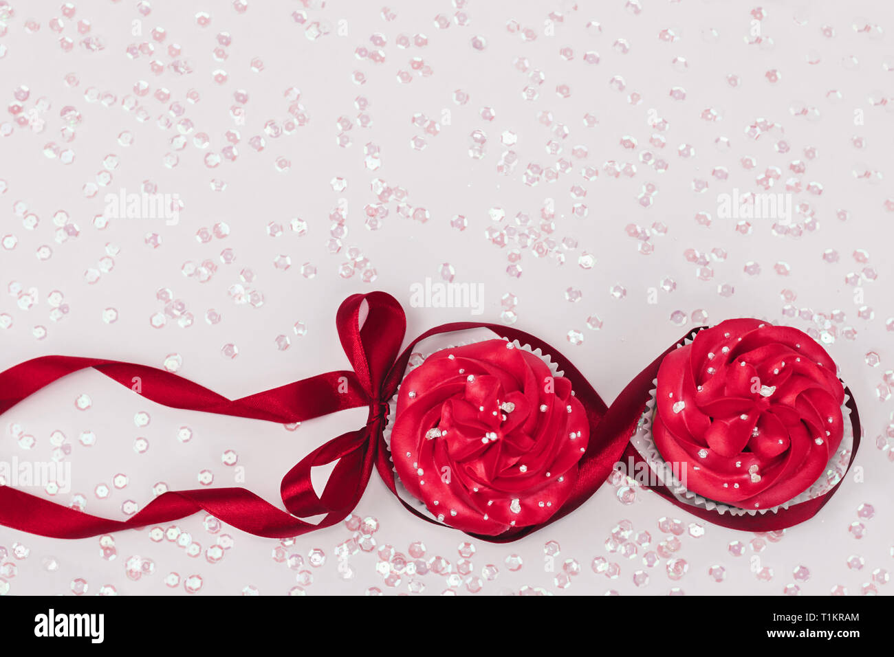 Two cupcakes with red icing decorated with red ribbon with a bow on ...