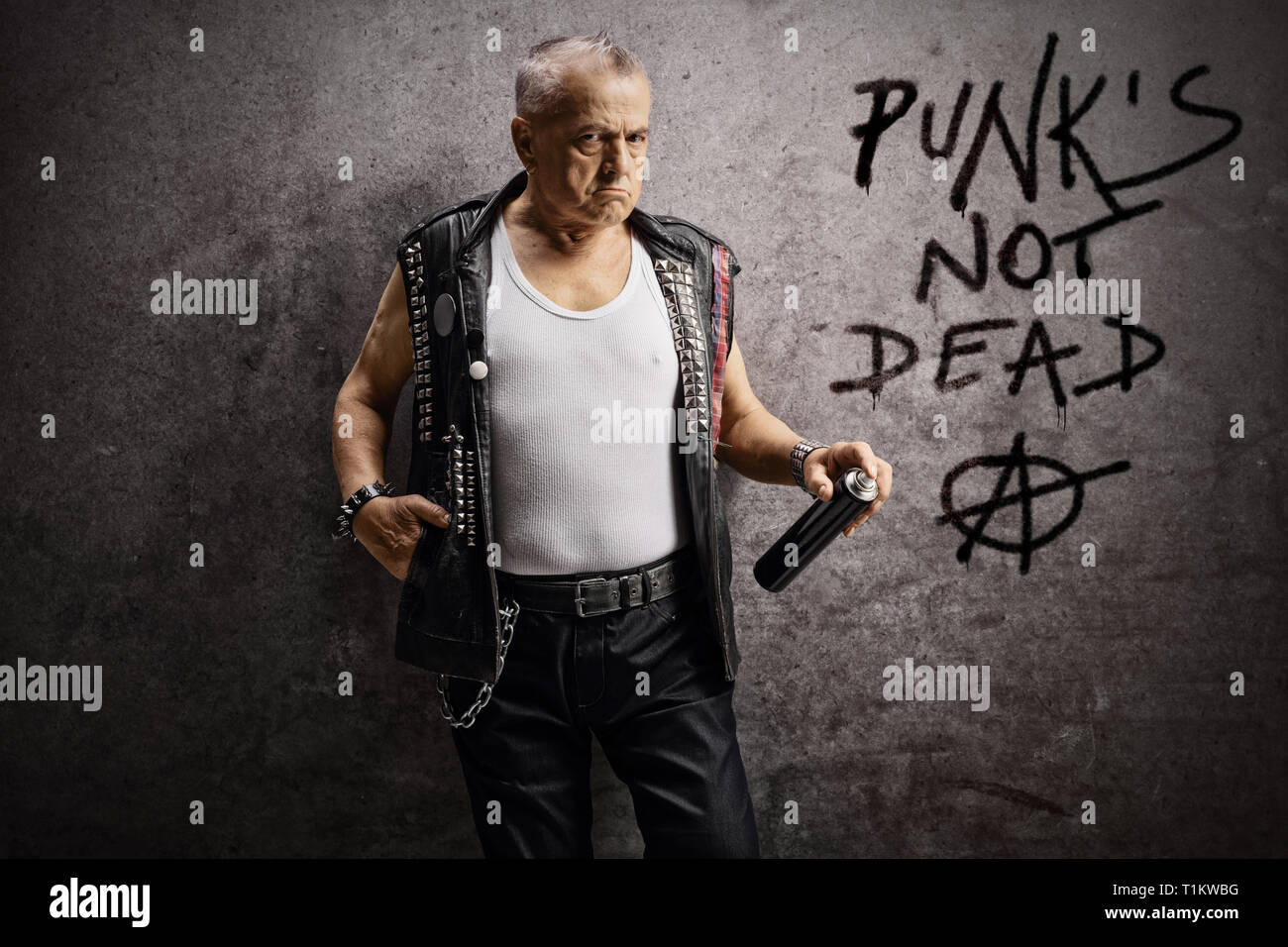 Mature male punker holding a wall spray and leaning against a rusty ...
