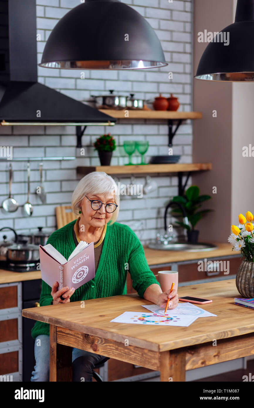 Attractive aged female considering vedic tables sitting at kitchen ...