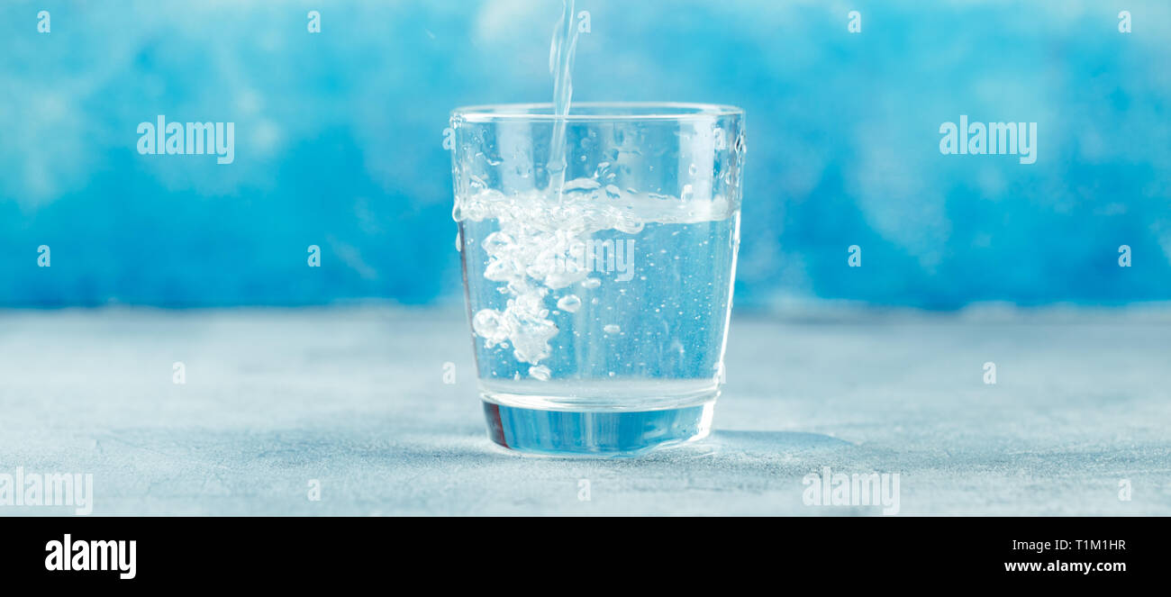 Pouring clear water from bottle into glass on blue background Stock ...