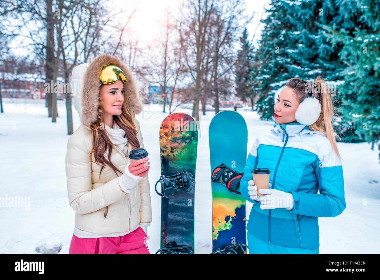 Two girls breathe winter woods resort. Against background snow boards ...