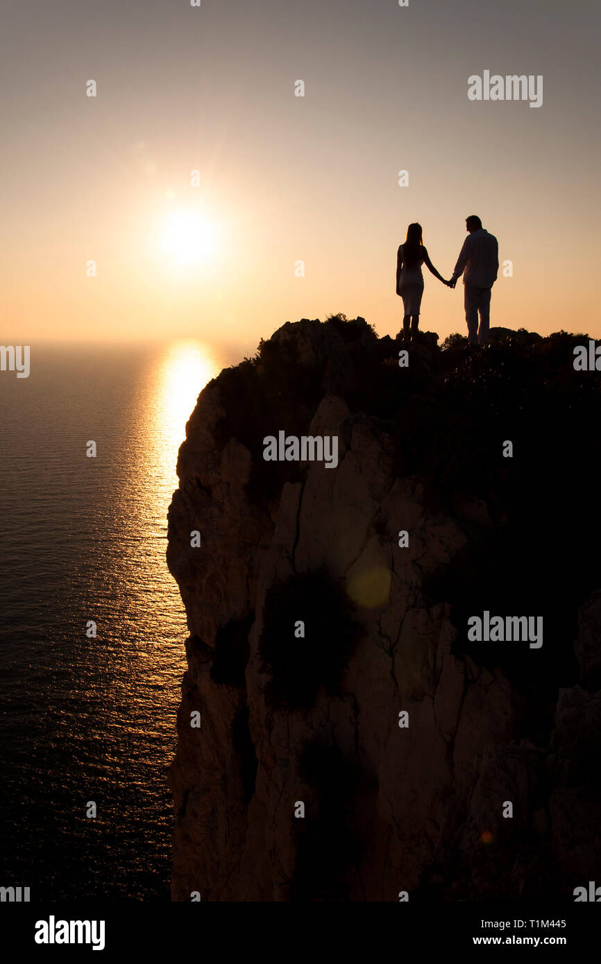 Silhouettes of couple in love holding by hands, standing on rocky cliff ...