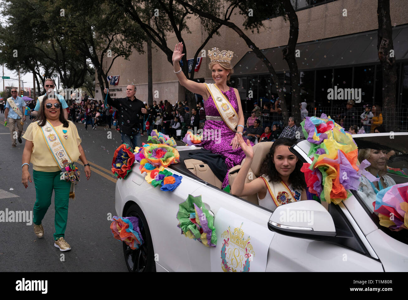 Young woman wearing crown sits on back of convertible car and waves to ...