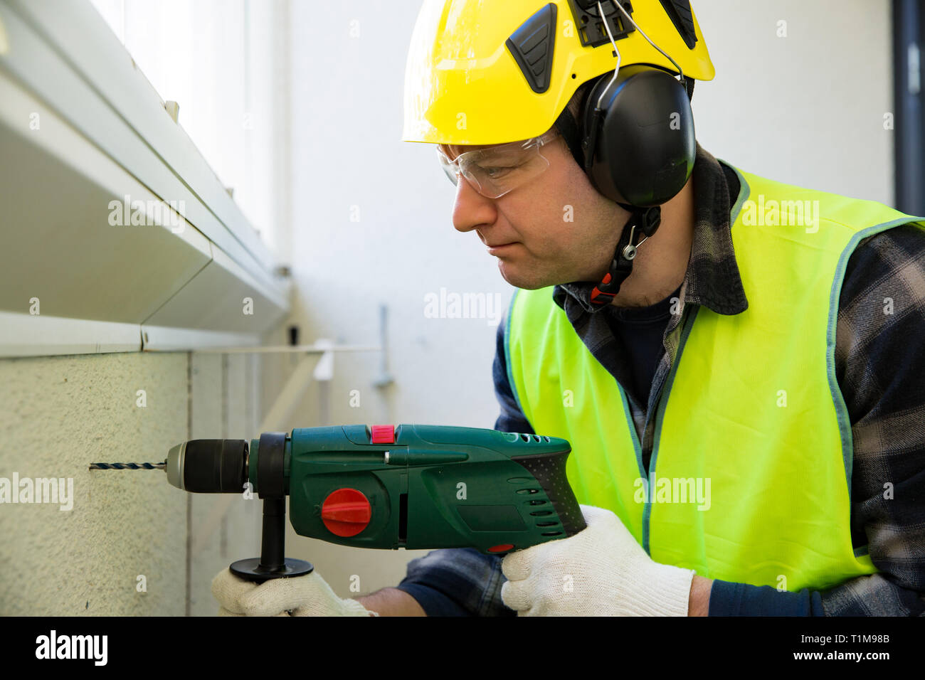 Male construction worker in hard hat drilling concrete wall with a ...