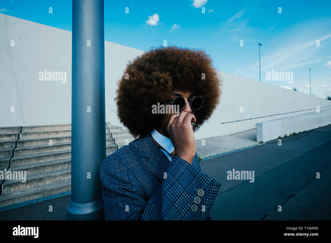 Well-dressed young man with afro smoking cigarette on urban sidewalk ...
