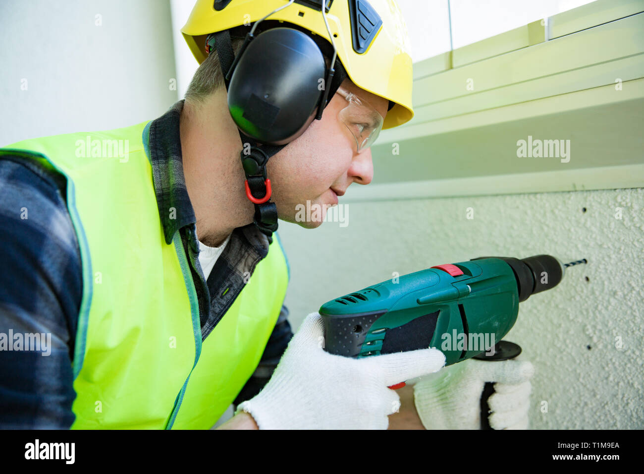 Male construction worker in hard hat drilling concrete wall with a ...