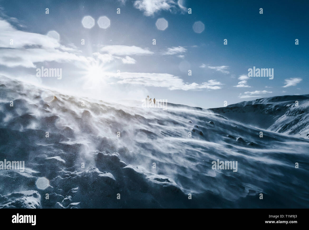People walking along sunny, windy, snow covered mountain, Reykjadalur ...