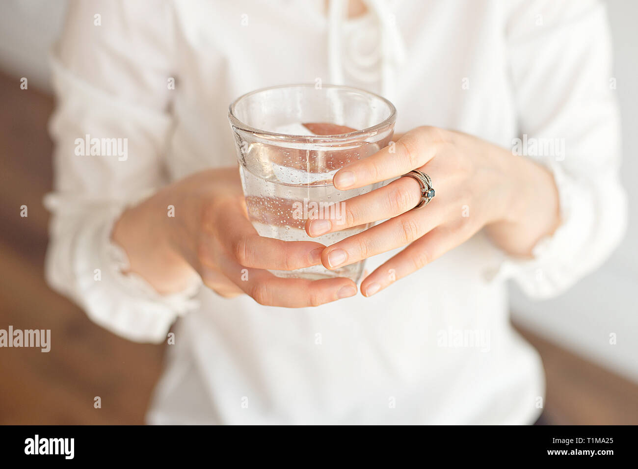Close-up of a woman's hand holding a cold glass of water and ice over a ...
