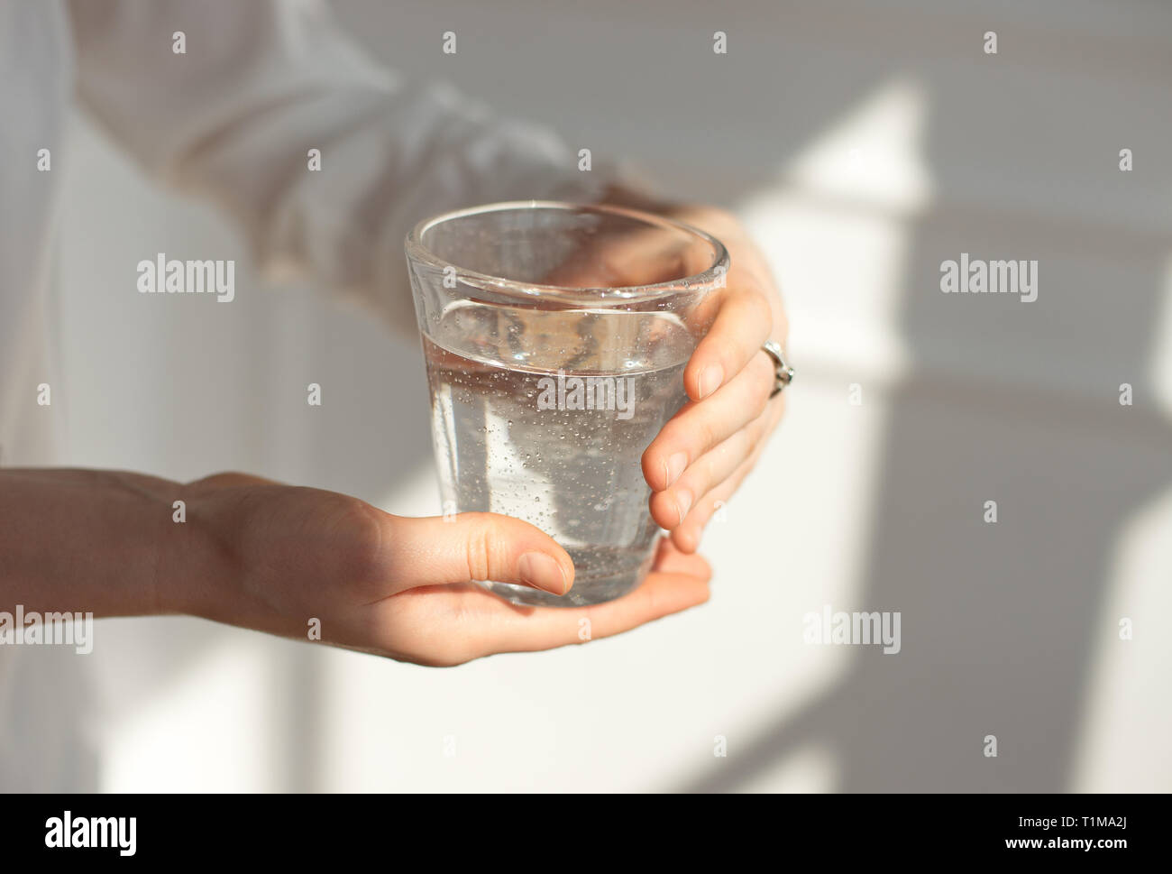 Close-up of a woman's hand holding a cold glass of water and ice over a ...