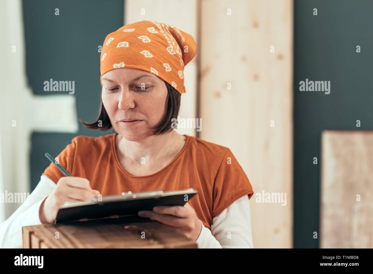 Female carpenter writing DIY project notes after finishing wooden crate ...