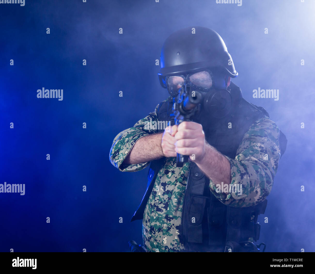 Soldier in army fatigues wearing gas mask holding assault rifle in haze ...