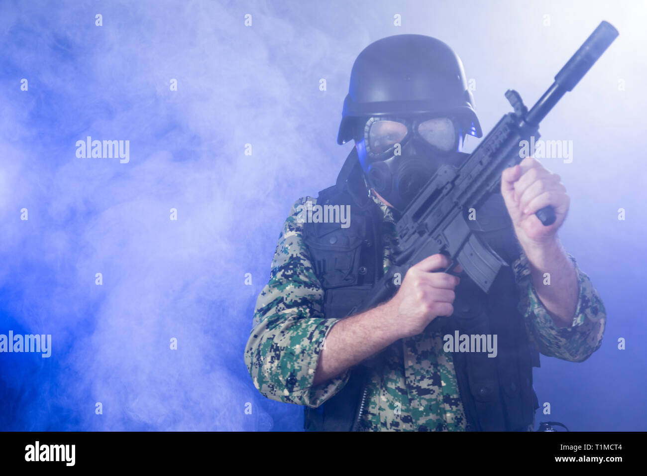 Soldier in army fatigues wearing gas mask holding assault rifle in haze ...