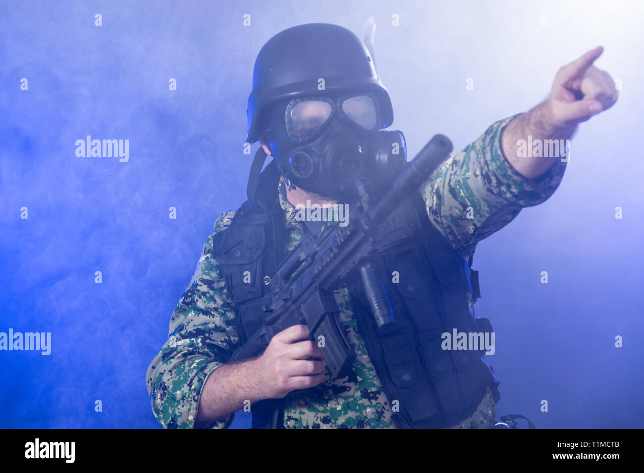 Soldier in army fatigues wearing gas mask holding assault rifle, points ...