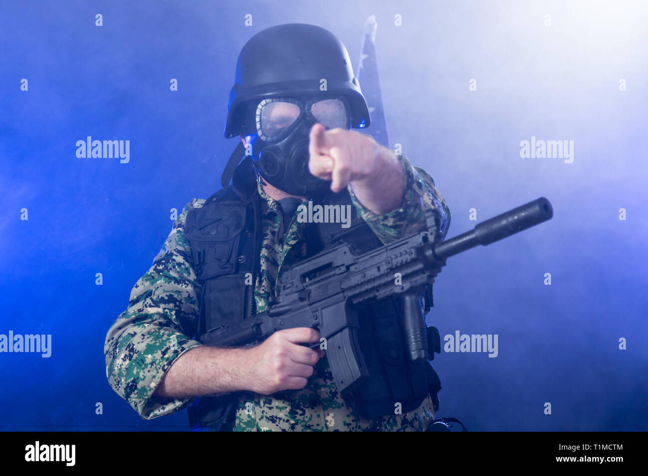 Soldier in army fatigues wearing gas mask holding assault rifle, points ...