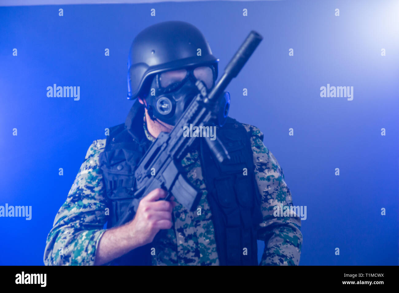 Soldier in army fatigues wearing gas mask holding assault rifle in haze ...