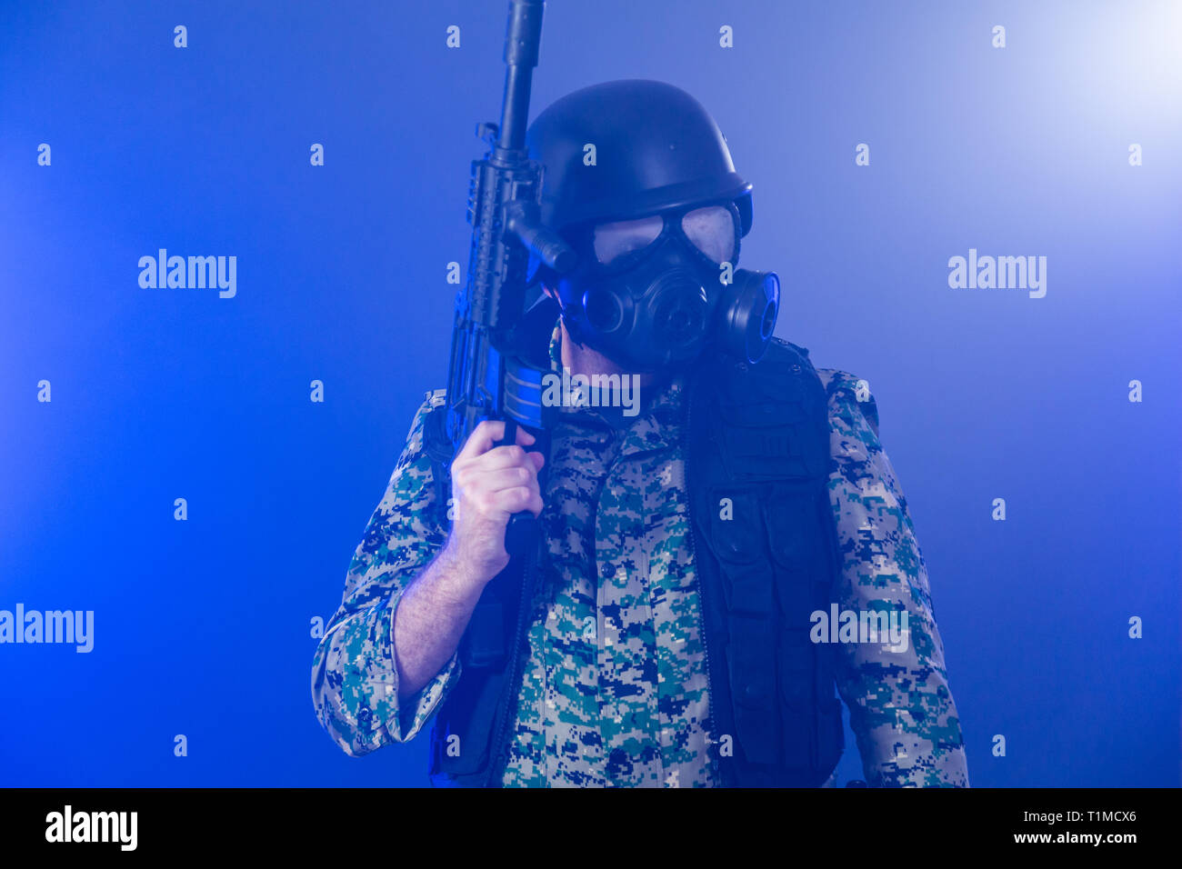 Soldier in army fatigues wearing gas mask holding assault rifle in haze ...
