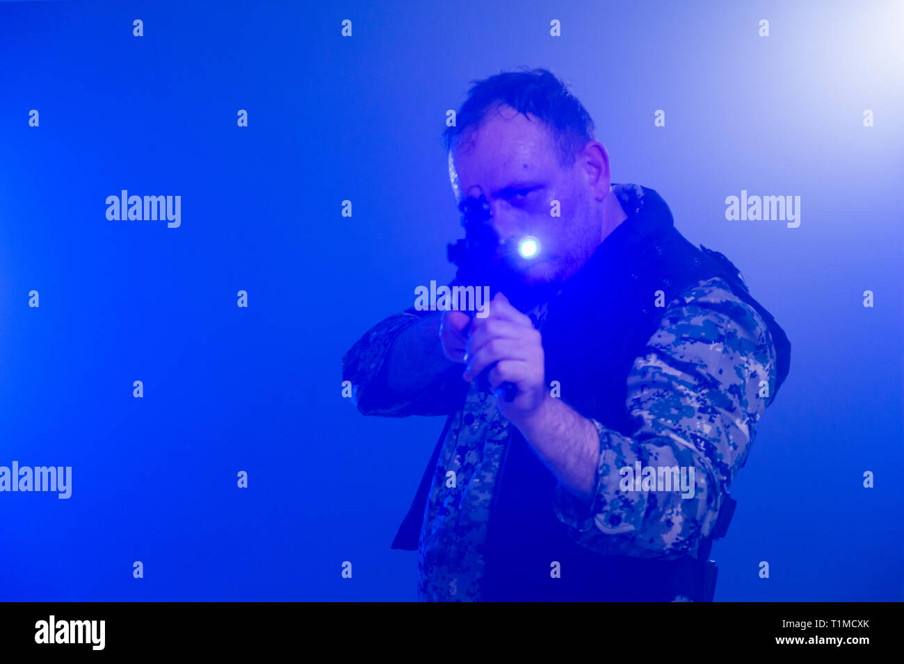 Soldier in army fatigues holding assault rifle in haze of blue smoke ...