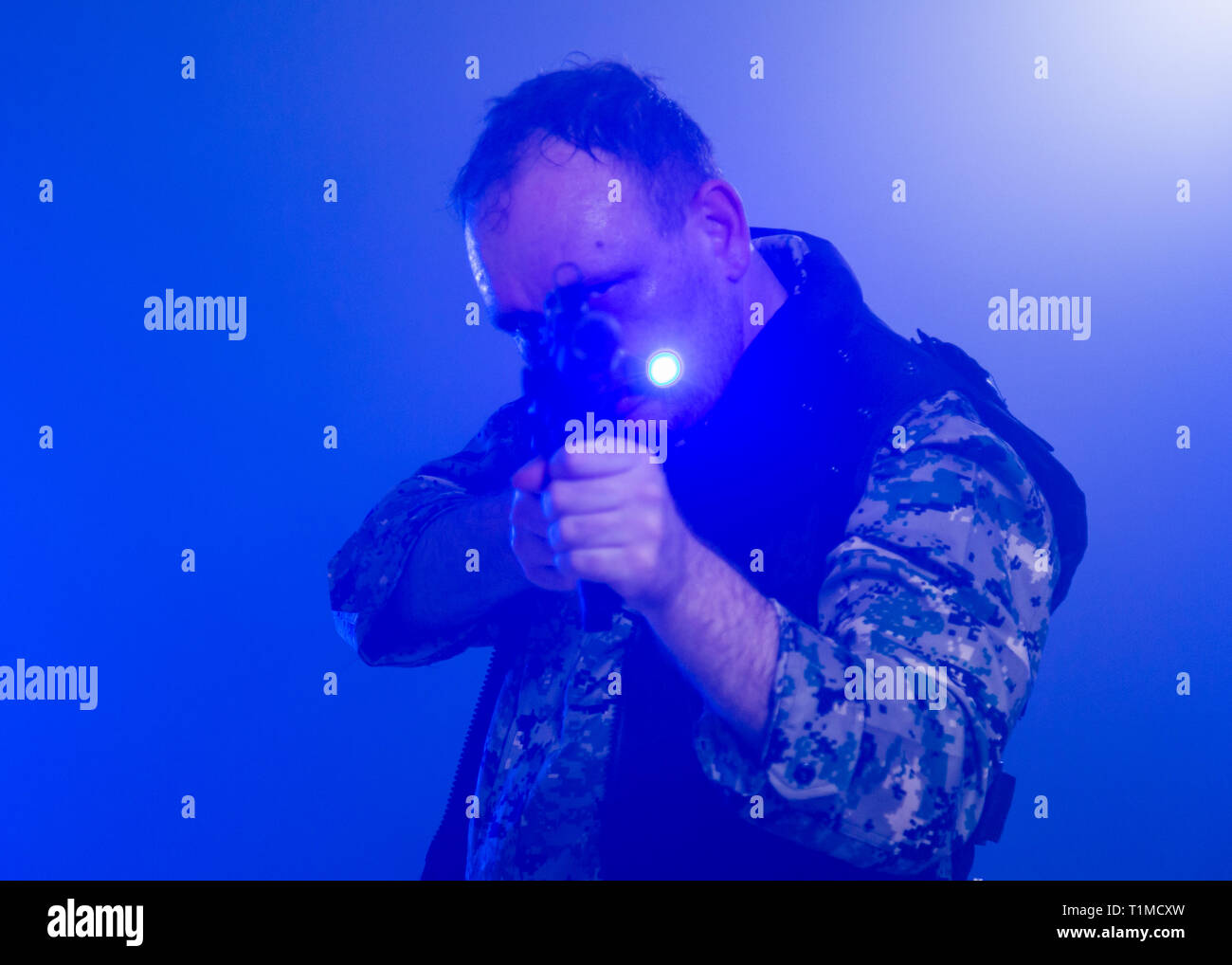 Soldier in army fatigues holding assault rifle in haze of blue smoke ...