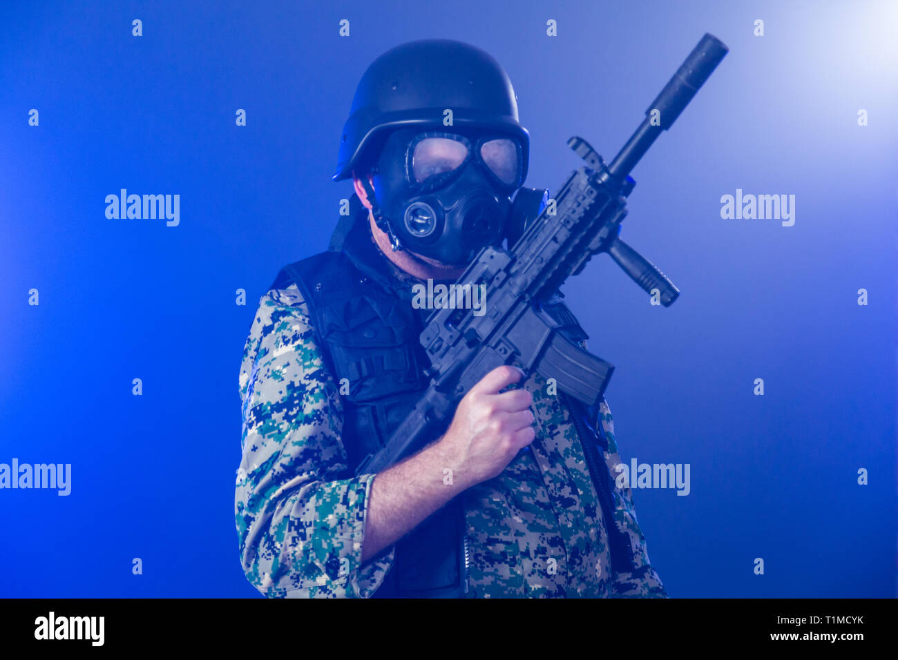 Soldier in army fatigues wearing gas mask holding assault rifle in haze ...