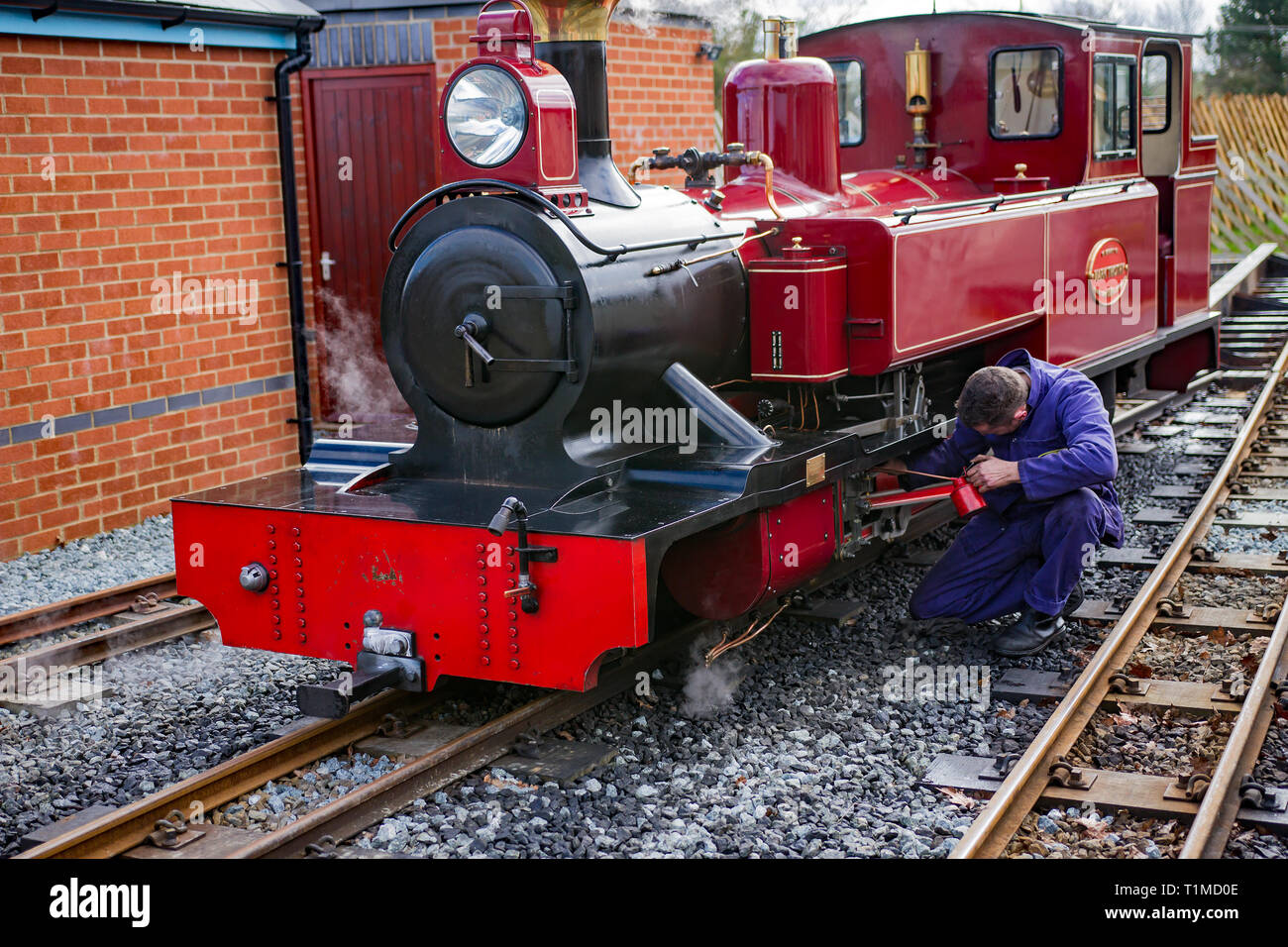 A train engineer in blue overalls crouching down and applying motor oil ...