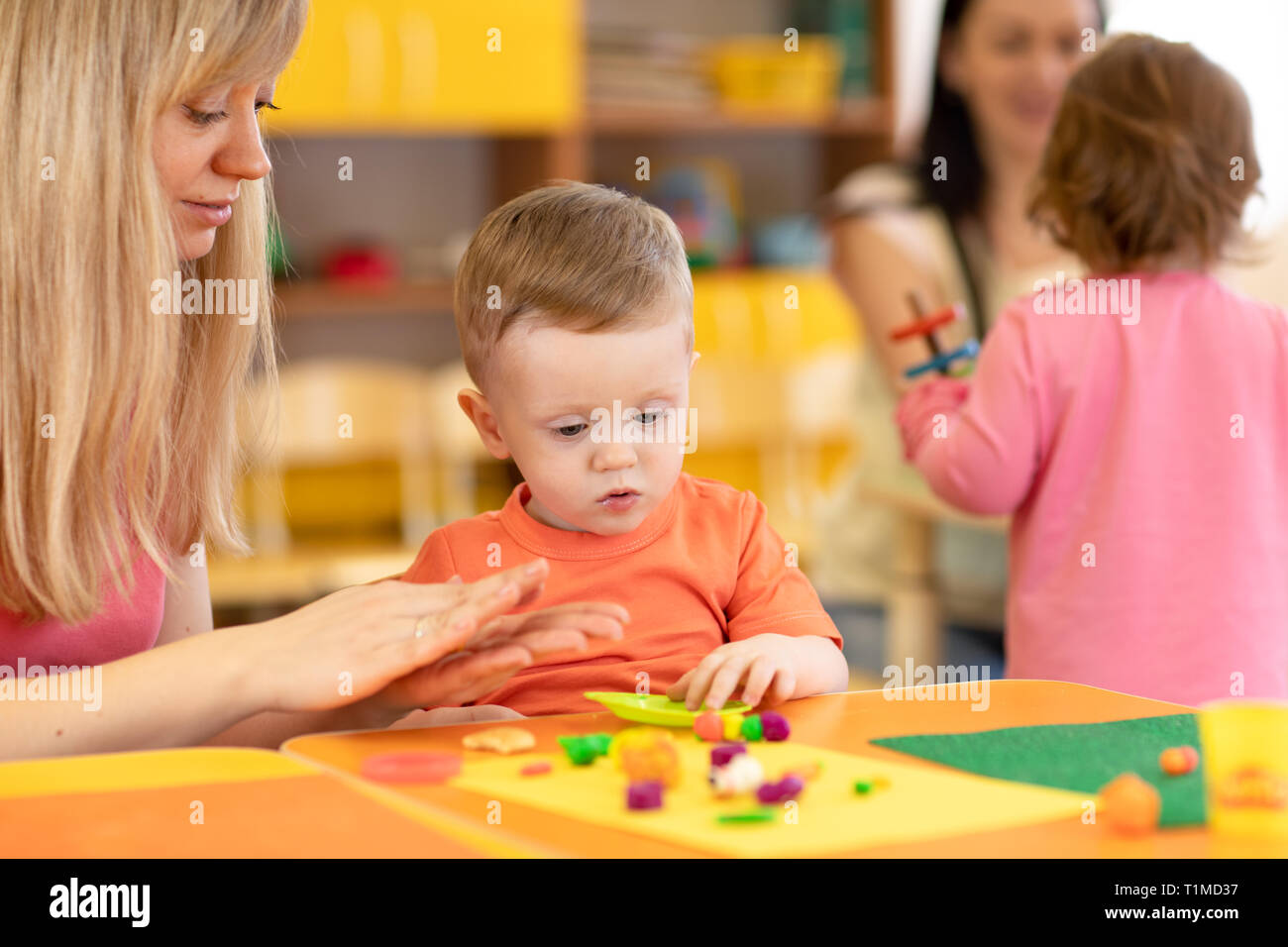 Kindergarten kid with teacher mould from plasticine on tablein nursery ...