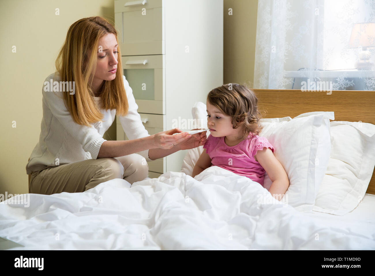 Mother measuring temperature of her ill kid. Sick child with high fever laying in bed and mother ...