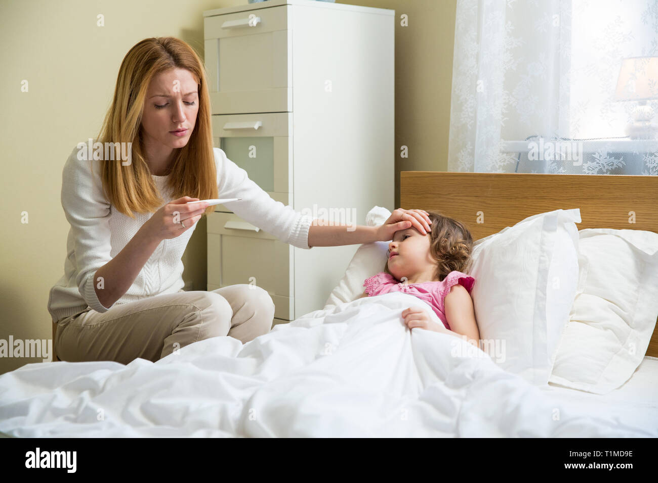 Mother measuring temperature of her ill kid. Sick child with high fever laying in bed and mother ...