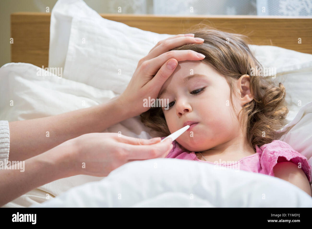 Mother measuring temperature of her ill kid. Sick child with high fever laying in bed and mother ...