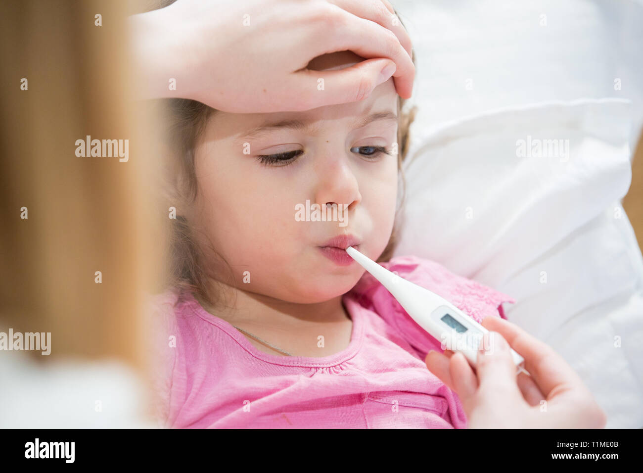 Mother measuring temperature of her ill kid. Sick child with high fever laying in bed and mother ...