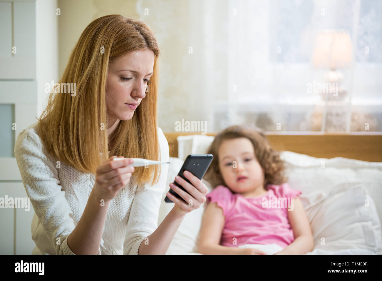 Mother measuring temperature of her ill kid. Sick child with high fever laying in bed and mother ...