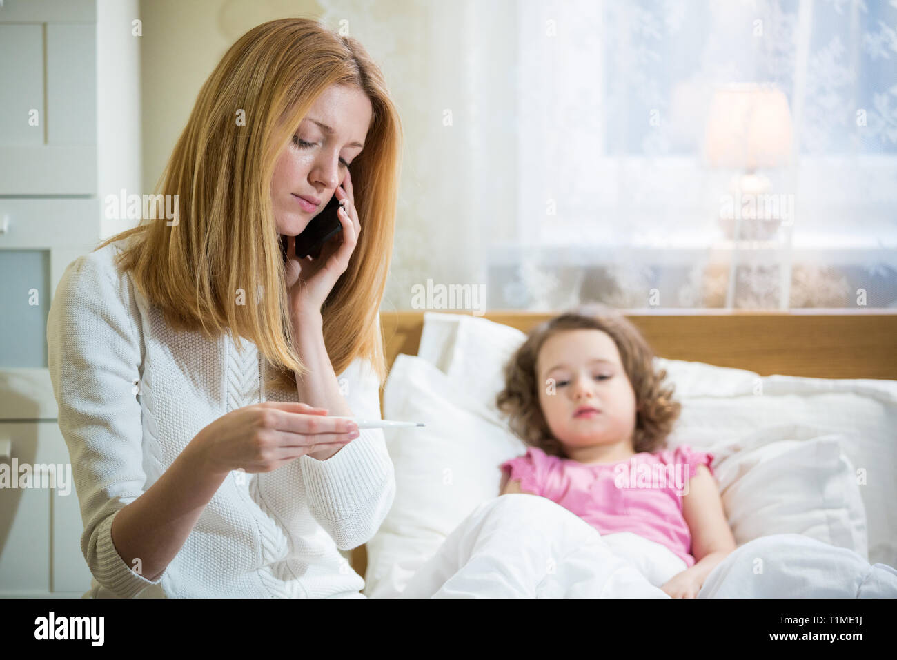 Mother measuring temperature of her ill kid. Sick child with high fever laying in bed and mother ...
