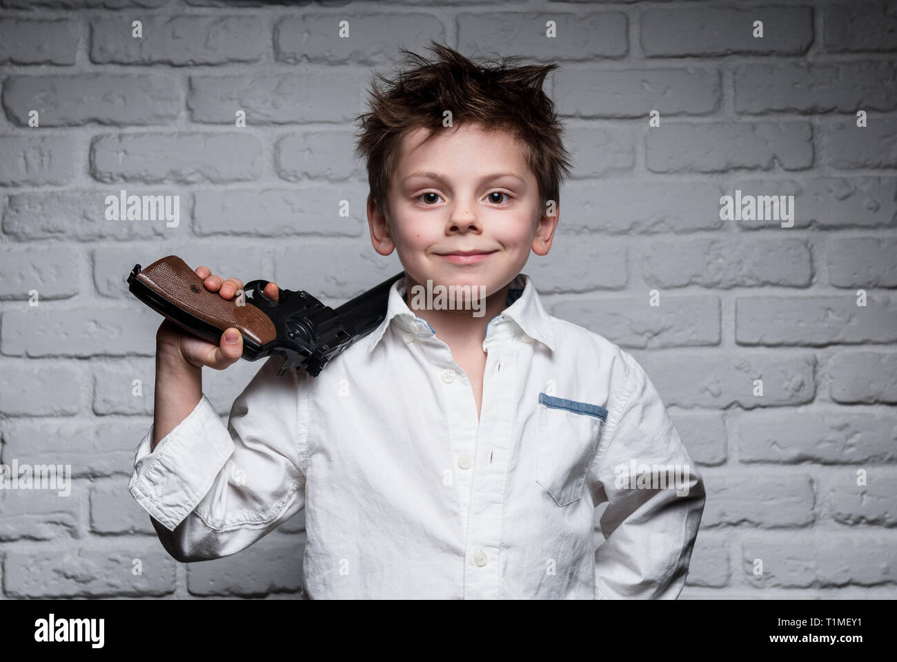 happy smiling small boy with big gun on brick wall background weapon ...