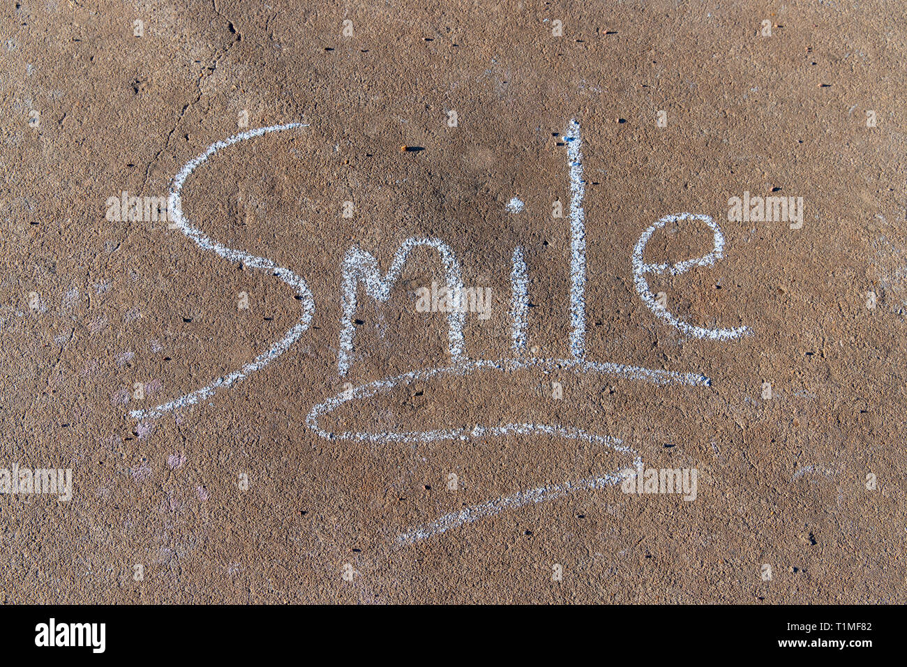the word Smile written with sidewalk chalk on gray concrete pavement ...