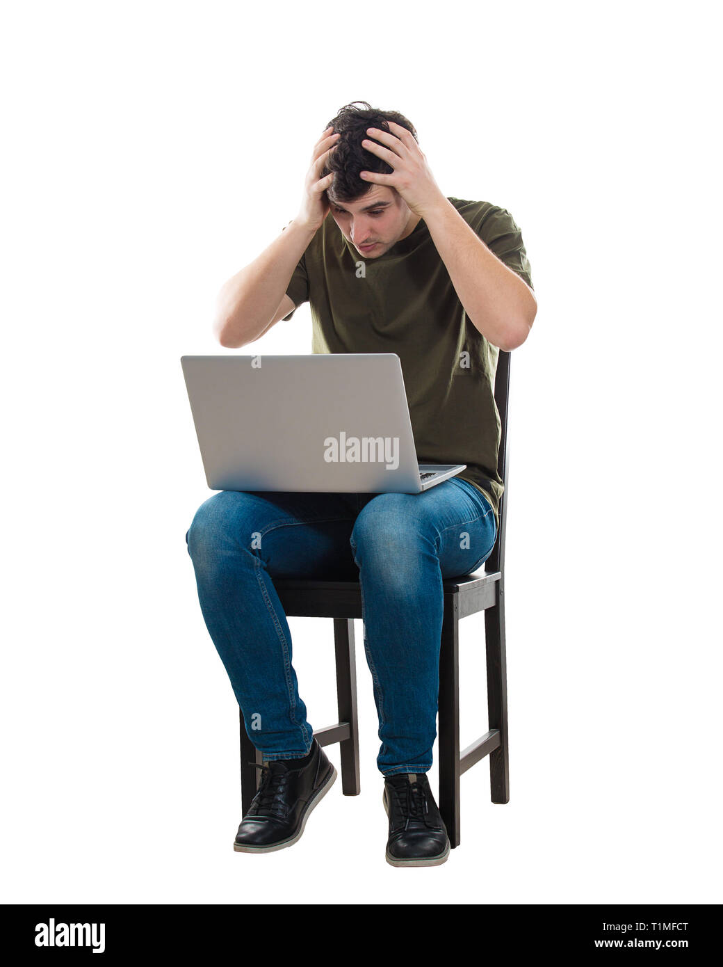 Upset and stressed young man using laptop seated on a chair, holding ...