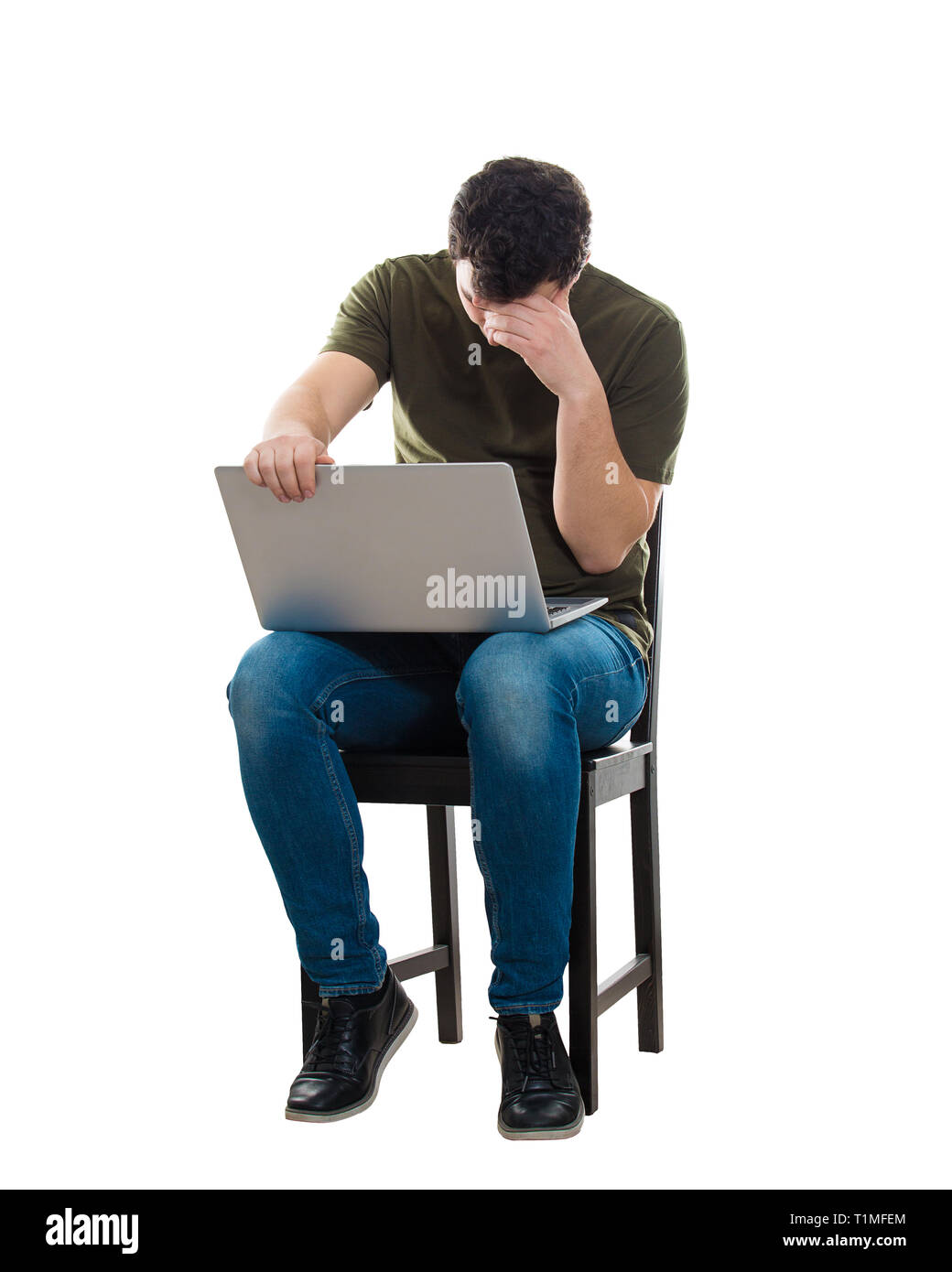 Angry young man with laptop on knees, hand to head looking disappointed ...