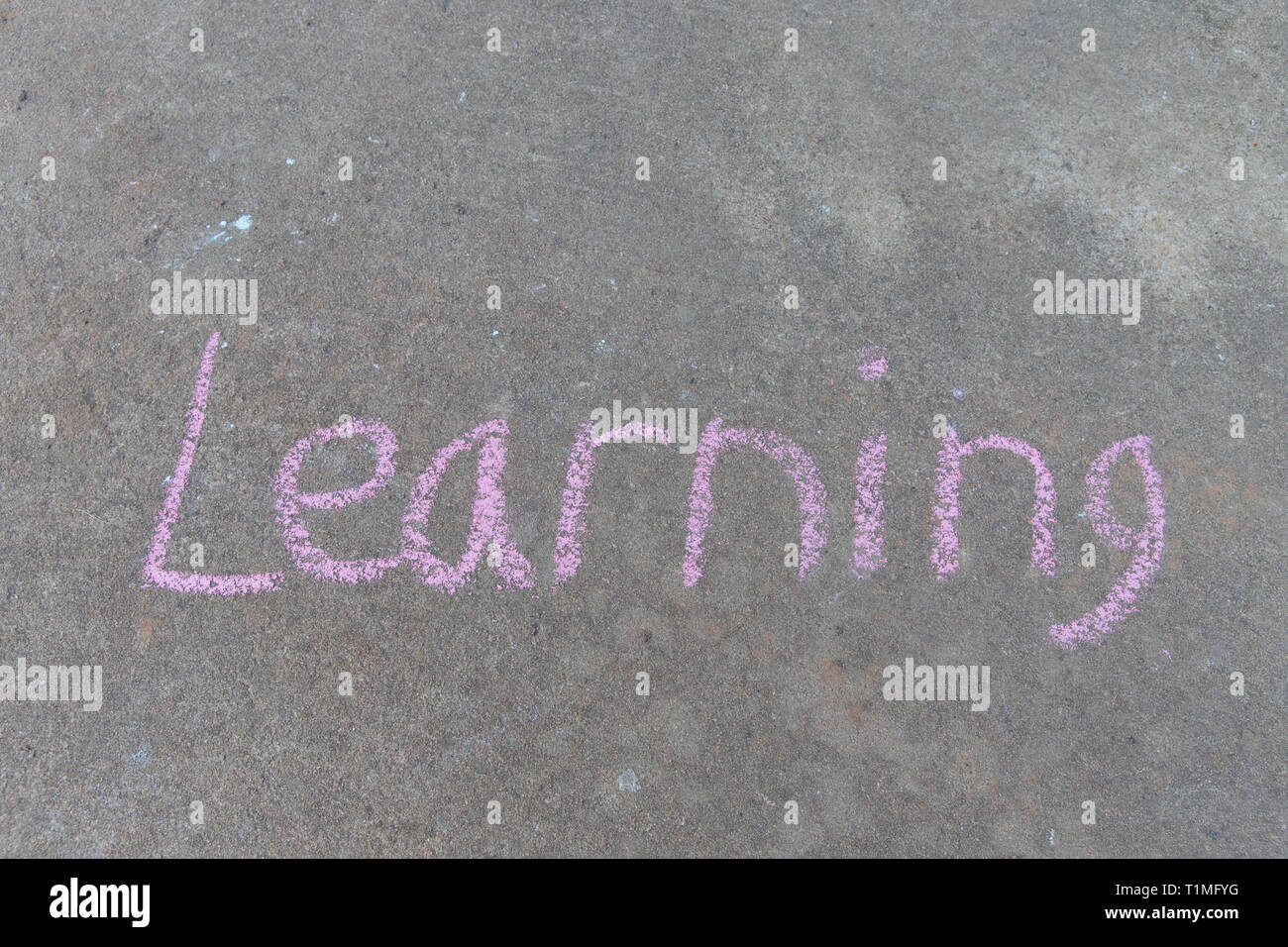 the word Learning written with pink sidewalk chalk on gray concrete ...