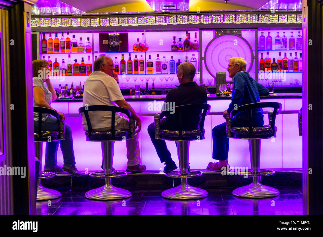 Adults sitting and drinking beer, wine, and alcohol at a colorful bar ...