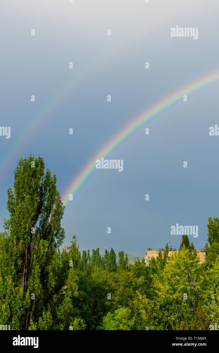 Natural double rainbow over green trees, city landscape Stock Photo - Alamy