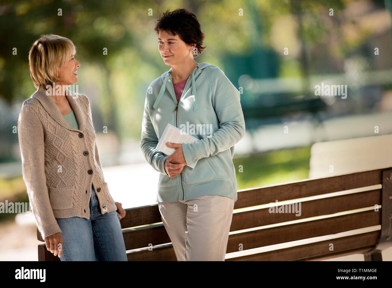 Two friends talking by a park bench Stock Photo - Alamy
