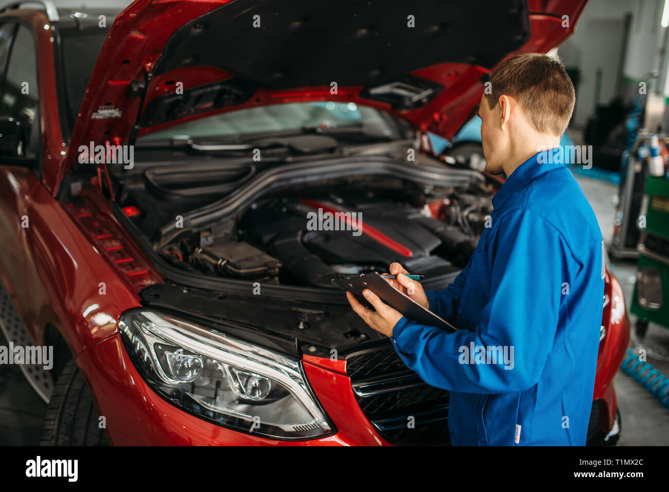 Technician with notebook, car with opened hood Stock Photo - Alamy