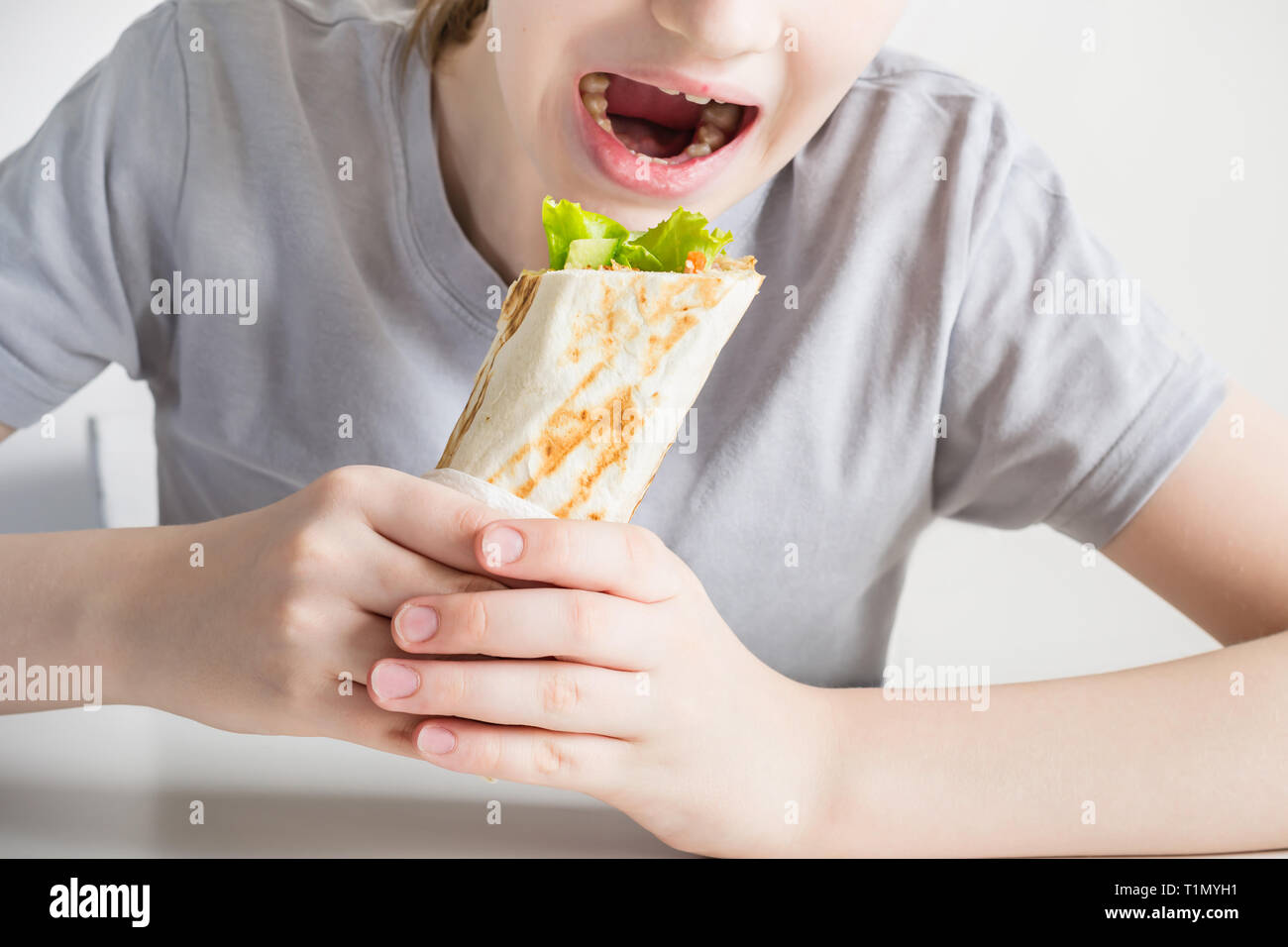 Teen boy eating shawarma sandwich roll close-up. Selective focus on ...